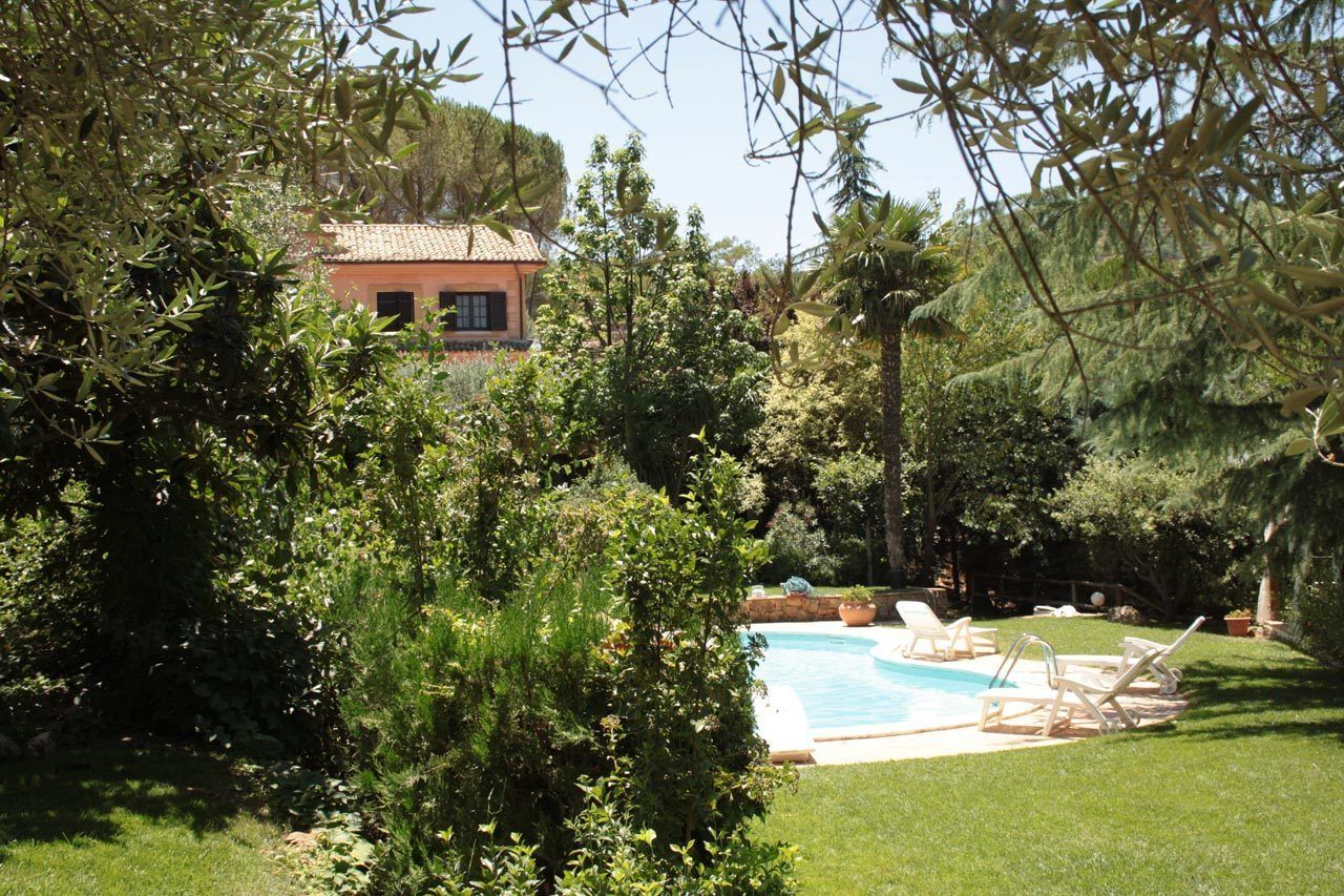 Piscina com espreguiçadeiras, rodeada por vegetação exuberante e um edifício ao fundo.