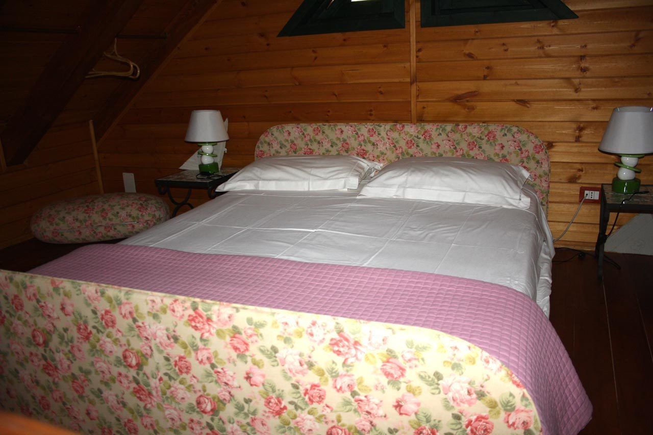 Um quarto de sótão aconchegante com teto inclinado de madeira, edredom estampado com flores e duas luminárias de cabeceira.