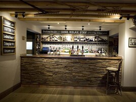 Uma área de bar com balcão de pedra, diversos tipos de bebidas e um letreiro com a inscrição 'DINE, RELAX, STAY'.