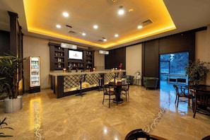 Um saguão de hotel com uma mesa de recepção, área de estar e uma grande janela.
