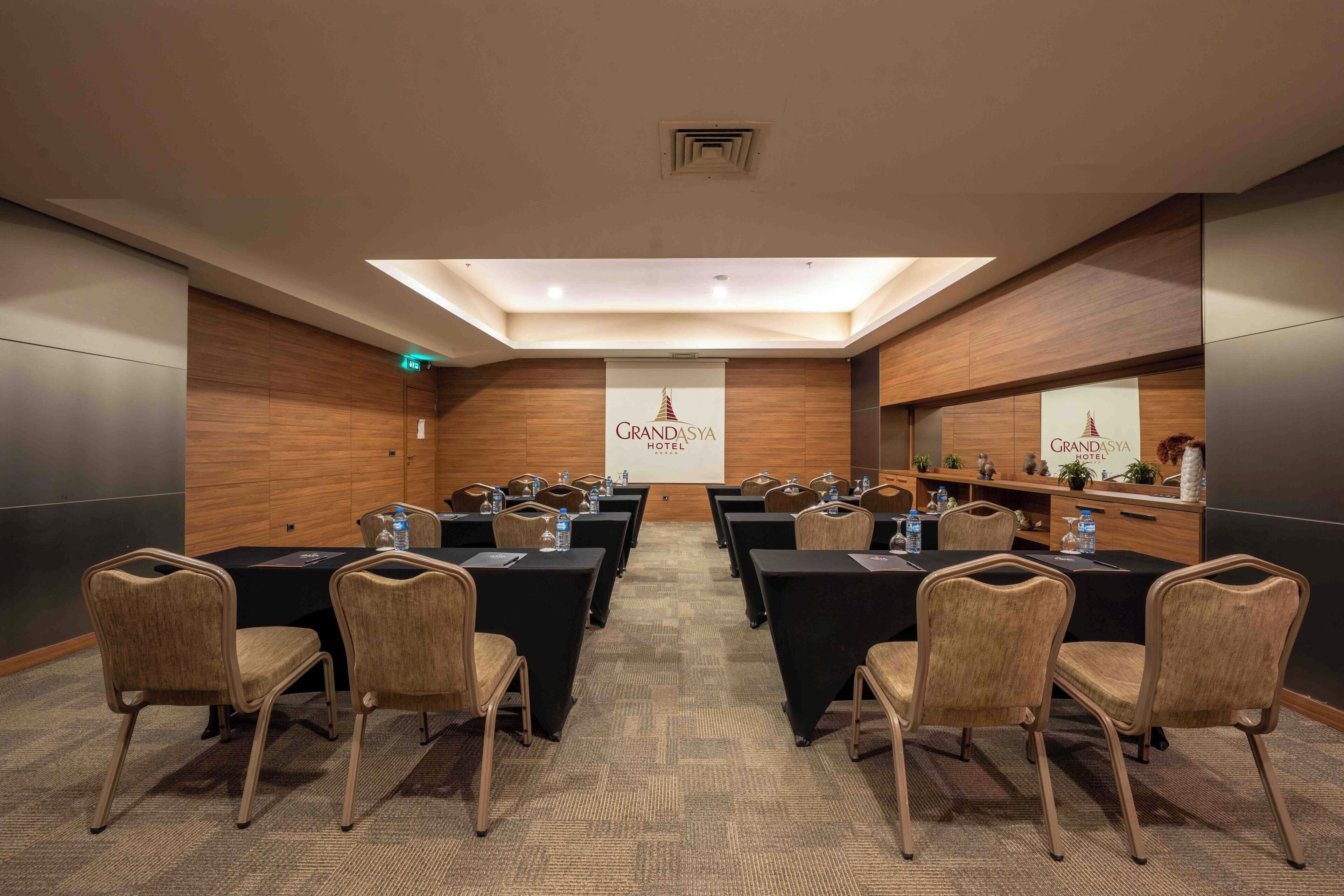Uma sala de conferência com uma mesa comprida, cadeiras e um banner do Grandasya Hotel.
