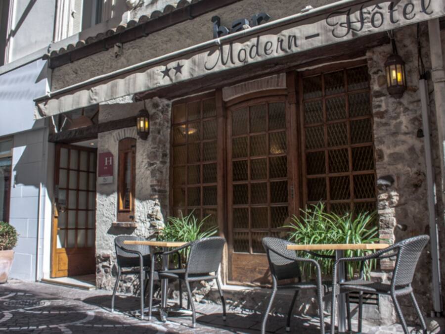 A stone building with a sign reading "Modern Hotel." There are outdoor tables and chairs, and a potted plant is visible.