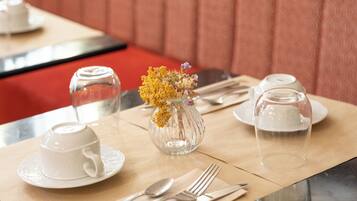 Uma mesa de jantar posta com xícaras brancas, um vaso de vidro com flores amarelas e um copo de vidro.