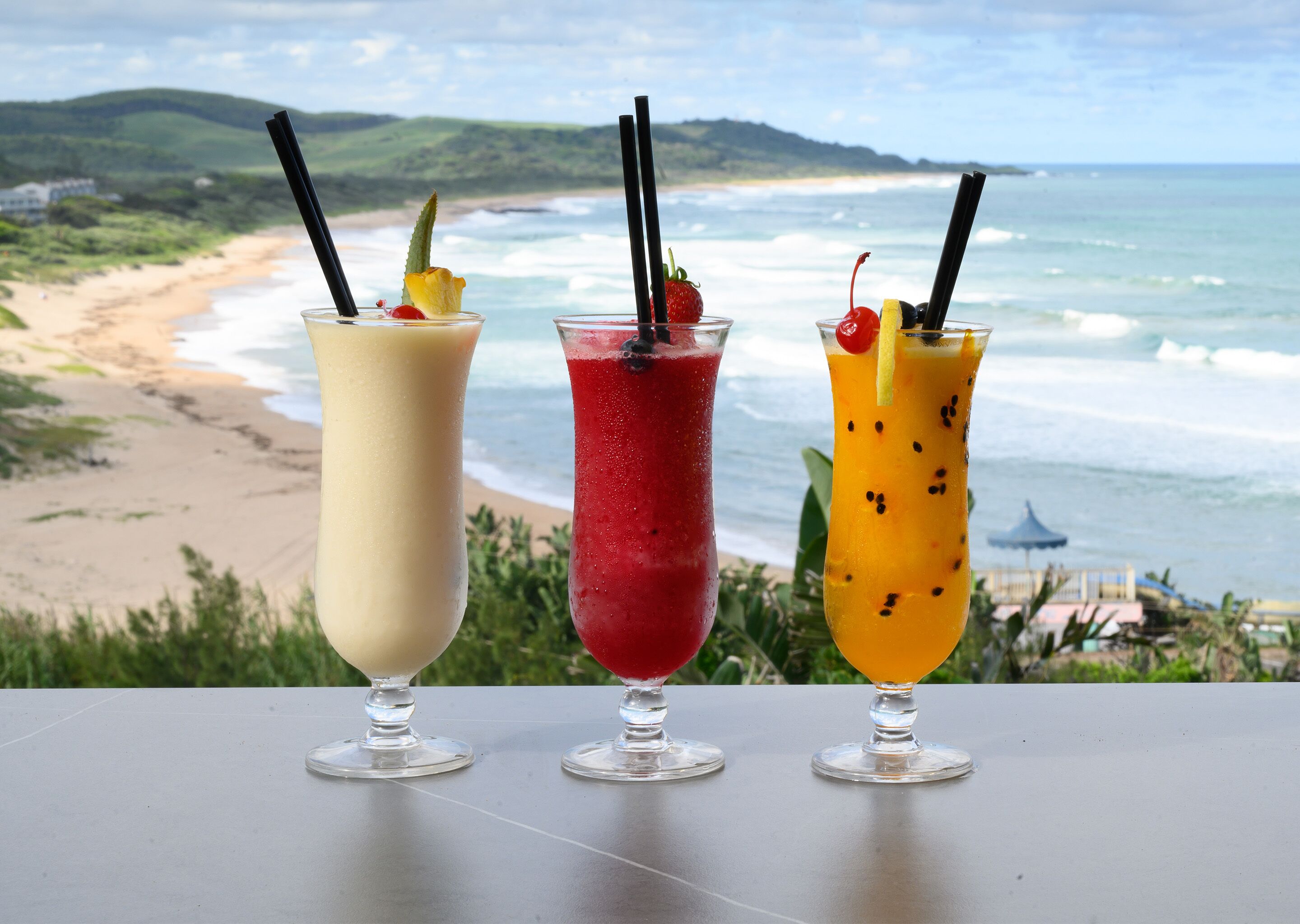 Três bebidas sobre uma mesa com vista para a praia.