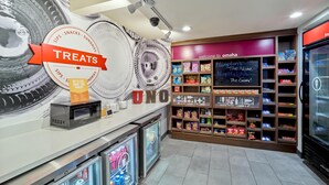 Um espaço de bebidas de serviço próprio, com sinalização para guloseimas, uma tela digital e uma geladeira abastecida com bebidas.
