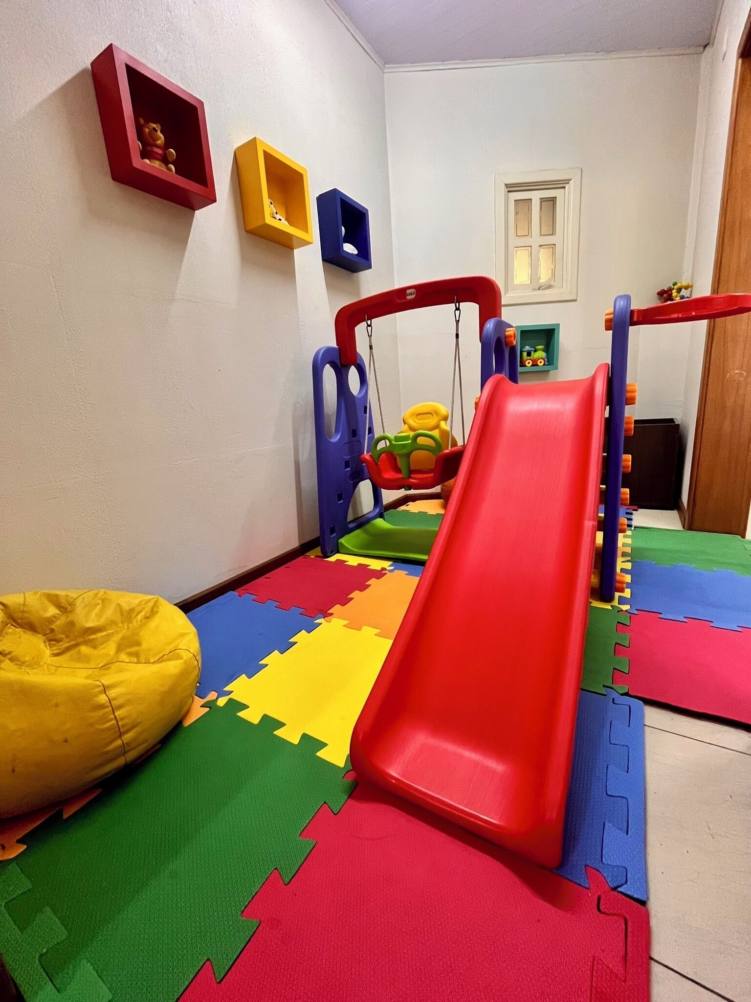 Uma sala de brinquedos com um escorregador, tapetes de espuma e caixas organizadoras na parede.