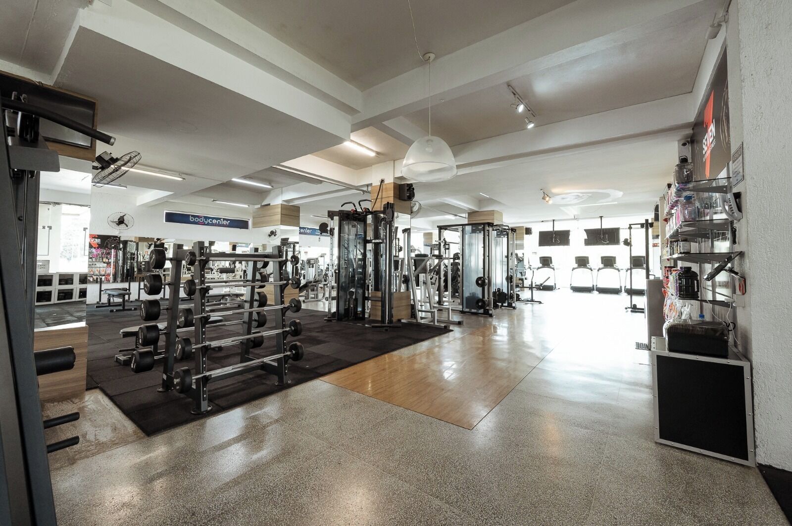 Academia com equipamentos de musculação, esteiras e um suporte fixado na parede.