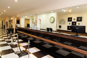 Uma área de recepção de hotel com um balcão de check-in, um relógio e uma placa indicando a localização do check-in.
