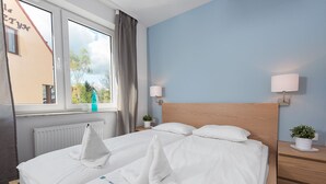 Quarto de hotel com uma cama grande, duas mesas de cabeceira com abajures, uma janela com cortinas e vista para o exterior.