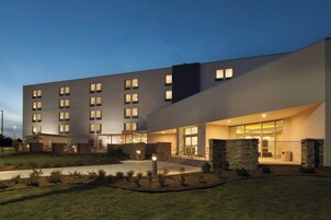 Um hotel moderno com telhado plano, várias janelas e uma entrada bem iluminada.