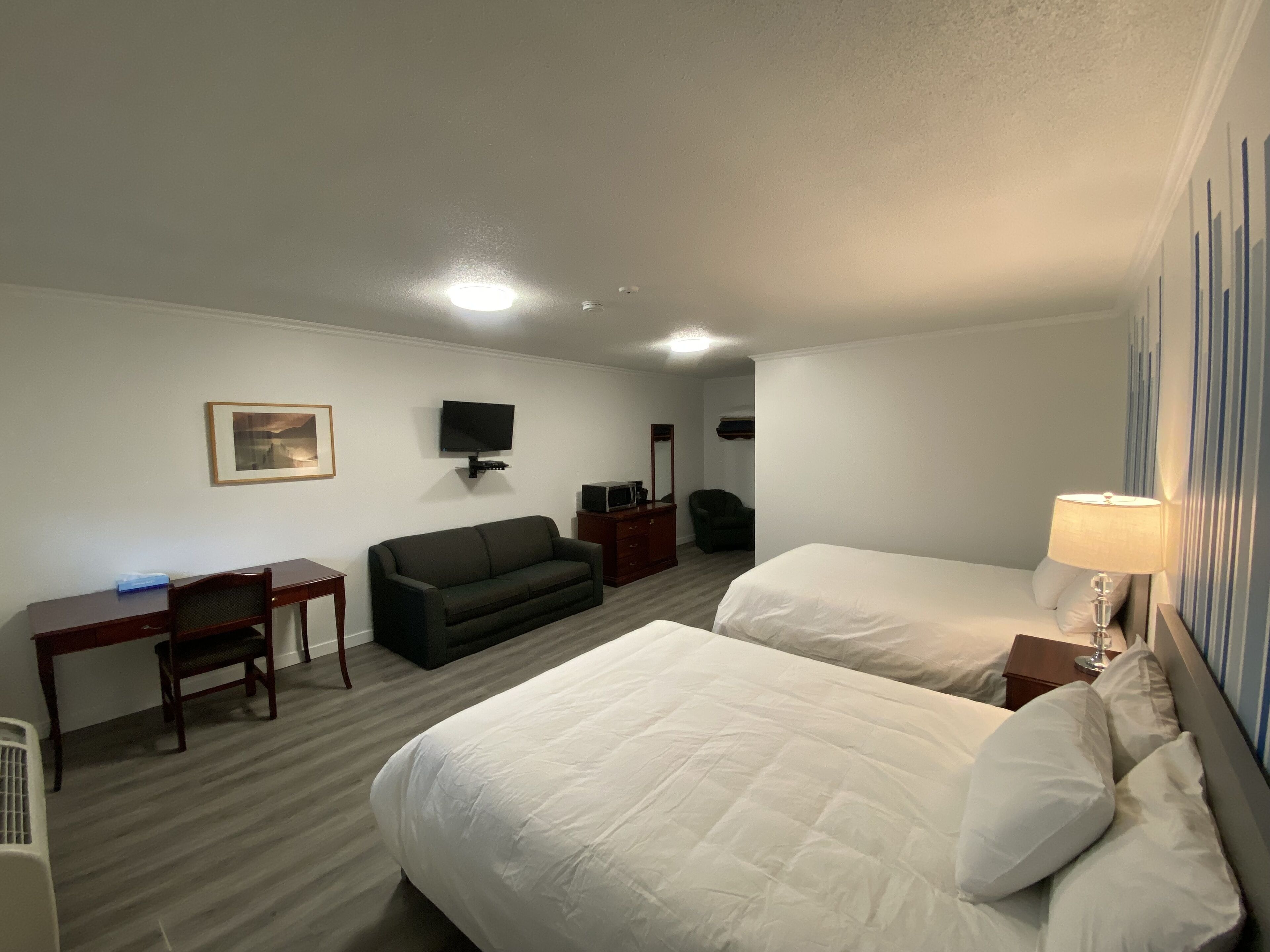Quarto de hotel com duas camas, uma escrivaninha, uma cadeira, uma televisão e um abajur.