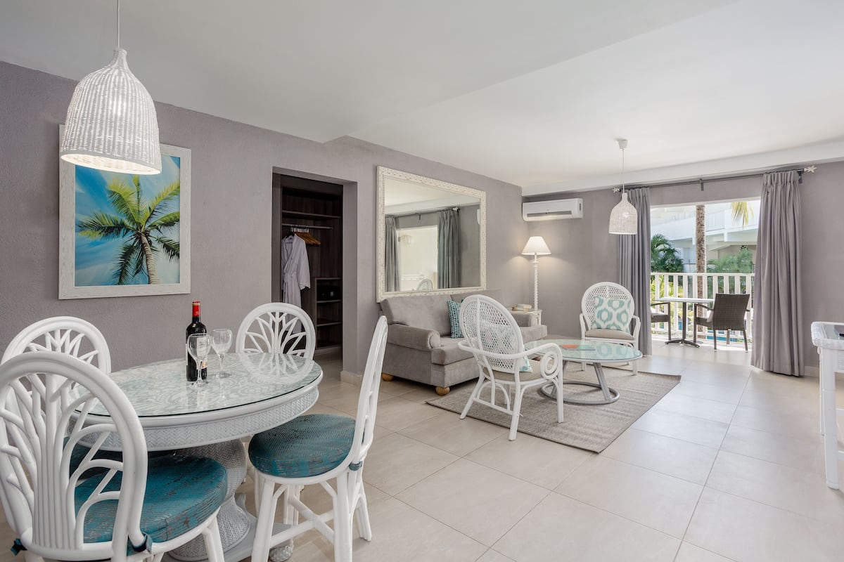 Quarto de hotel moderno com área de jantar, sofá e varanda com cortinas.