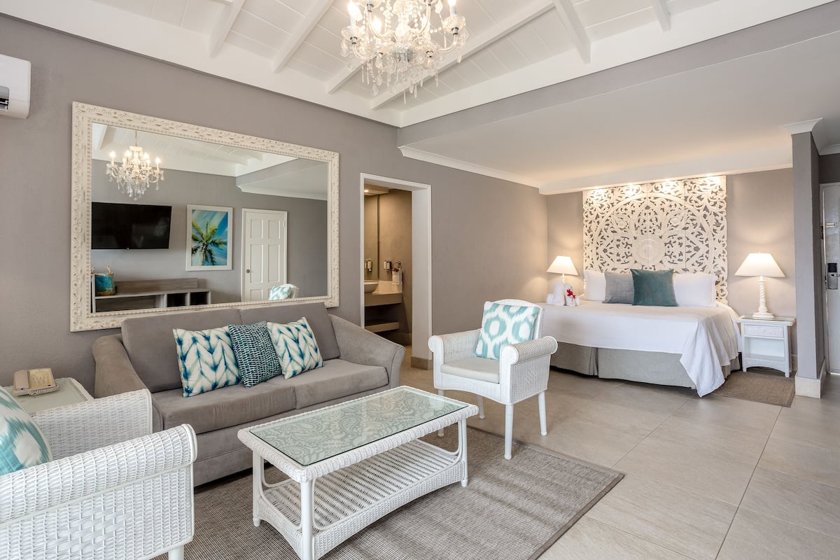 Quarto moderno com uma cama grande, um espaço de estar com mesa de centro de vidro e um espelho amplo.