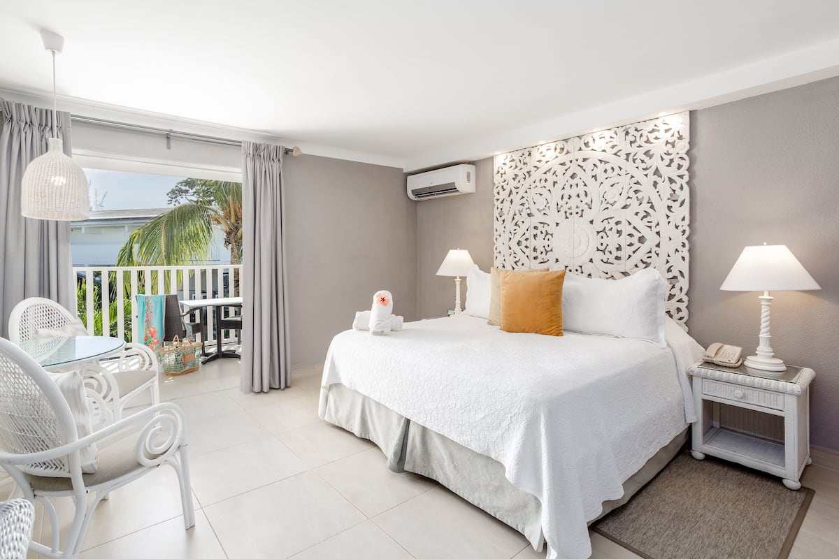 Quarto de hotel com cama, mesa de cabeceira e varanda com mesa e cadeiras.
