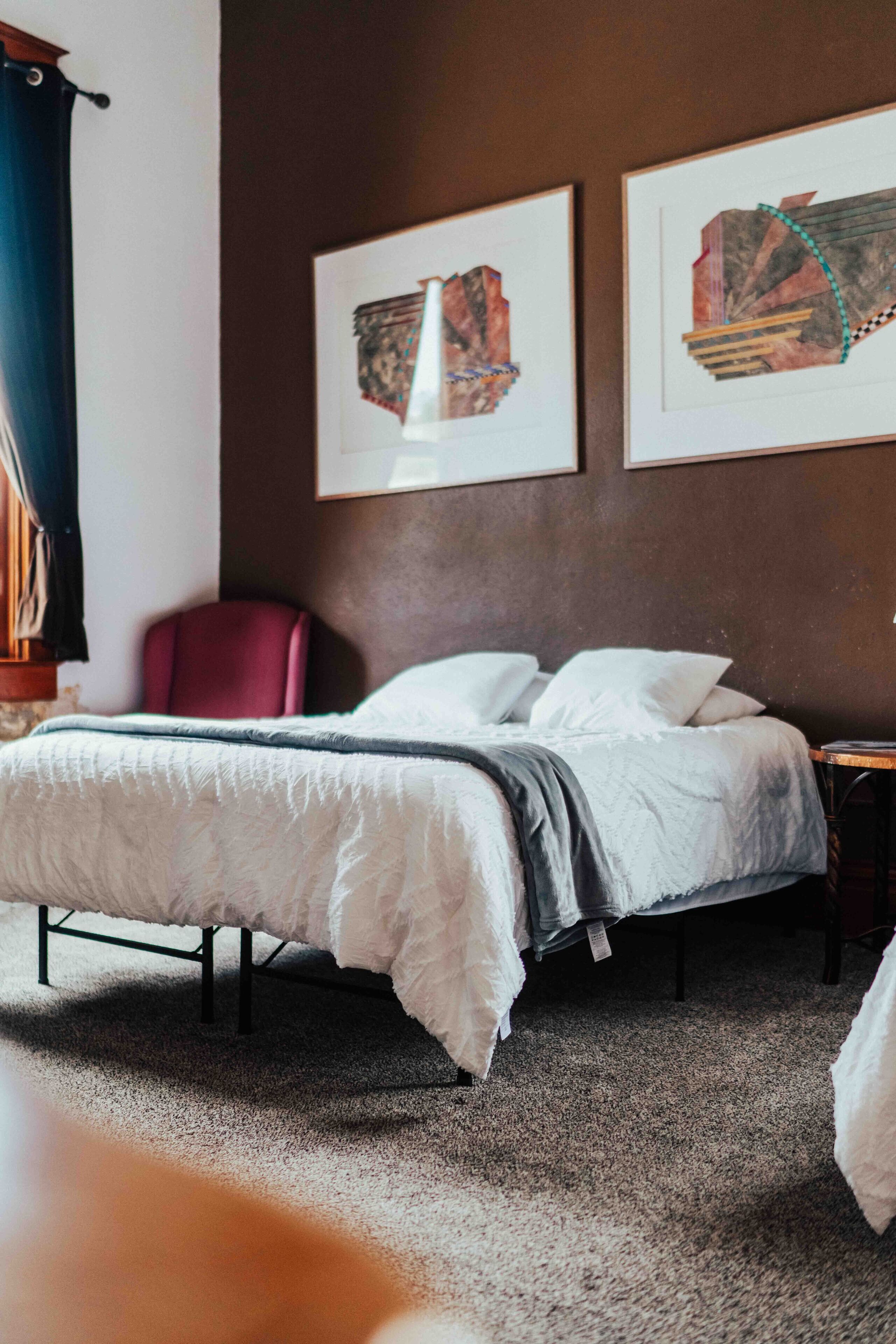 Quarto de hotel com uma cama, uma cadeira e duas obras de arte emolduradas na parede.