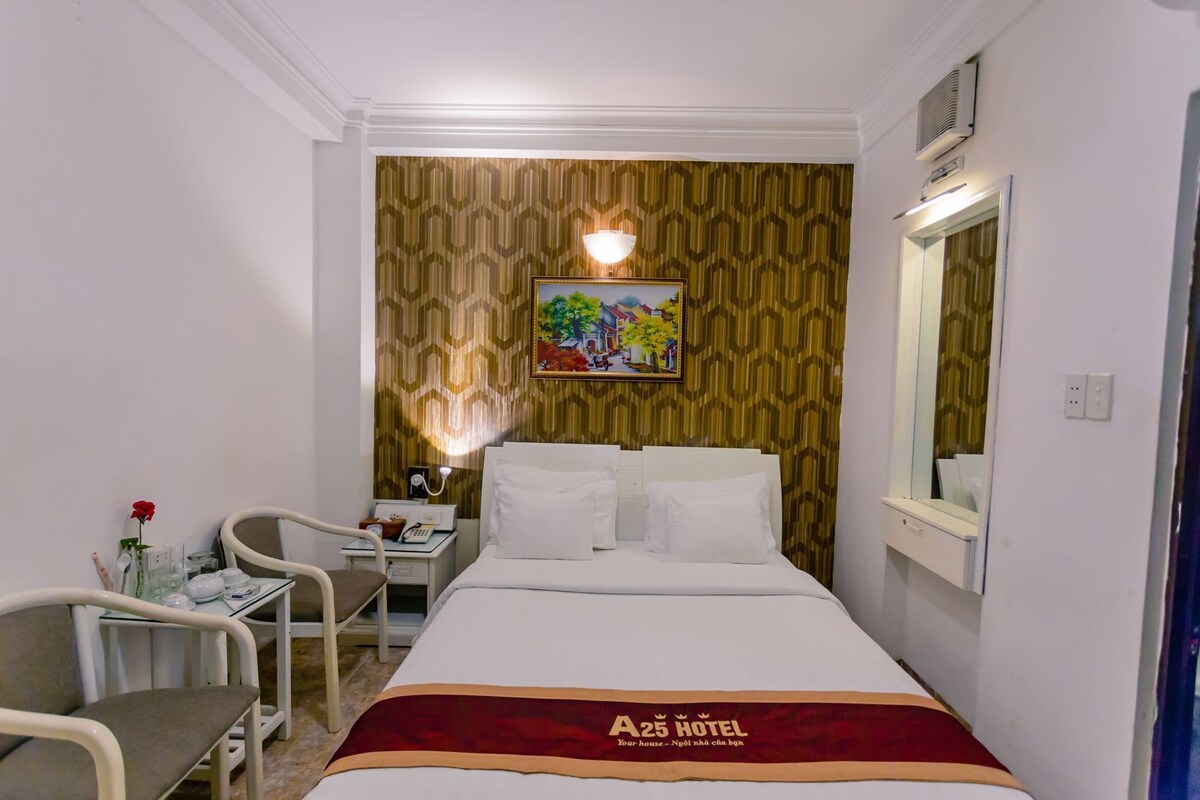 Quarto de hotel com cama, escrivaninha, cadeira, um quadro na parede e um espelho.