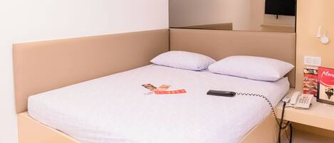 Cama bem arrumada com lençol branco e duas almofadas, um telefone ao lado da cama e uma revista sobre a cama.