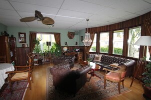 Uma sala de estar espaçosa com um amplo sofá de couro, cadeiras de madeira, uma mesa de jantar e um lustre.