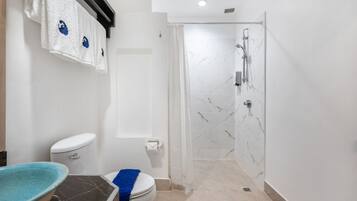 Uma casa de banho com sanita, lavatório e toalha azul, e zona de duche com parede de mármore.
