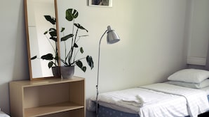 Quarto com duas camas de solteiro, uma mesa de cabeceira, um espelho, um vaso de planta, um abajur e um quadro na parede.