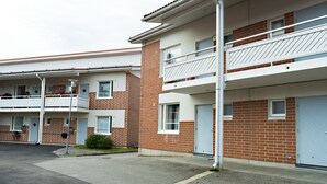 Um edifício de vários andares com fachada de tijolo, varandas brancas e um estacionamento à frente.