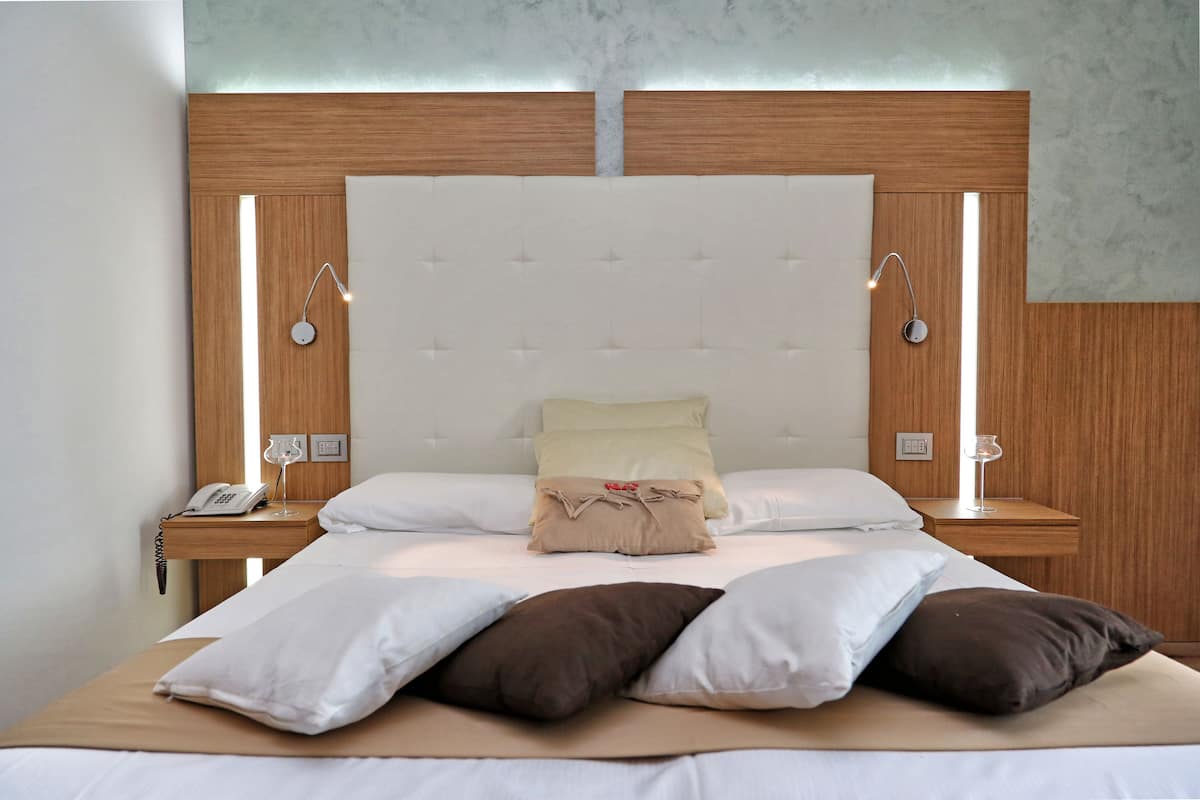 Uma cama bem arrumada com cabeceira de madeira, duas mesas de cabeceira com abajures e um telefone na mesa da esquerda.