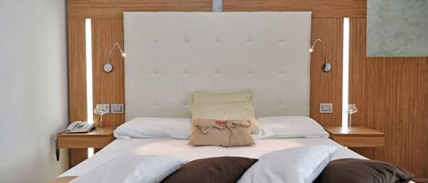Uma cama bem arrumada com cabeceira de madeira, duas mesas de cabeceira com abajures e um telefone na mesa da esquerda.