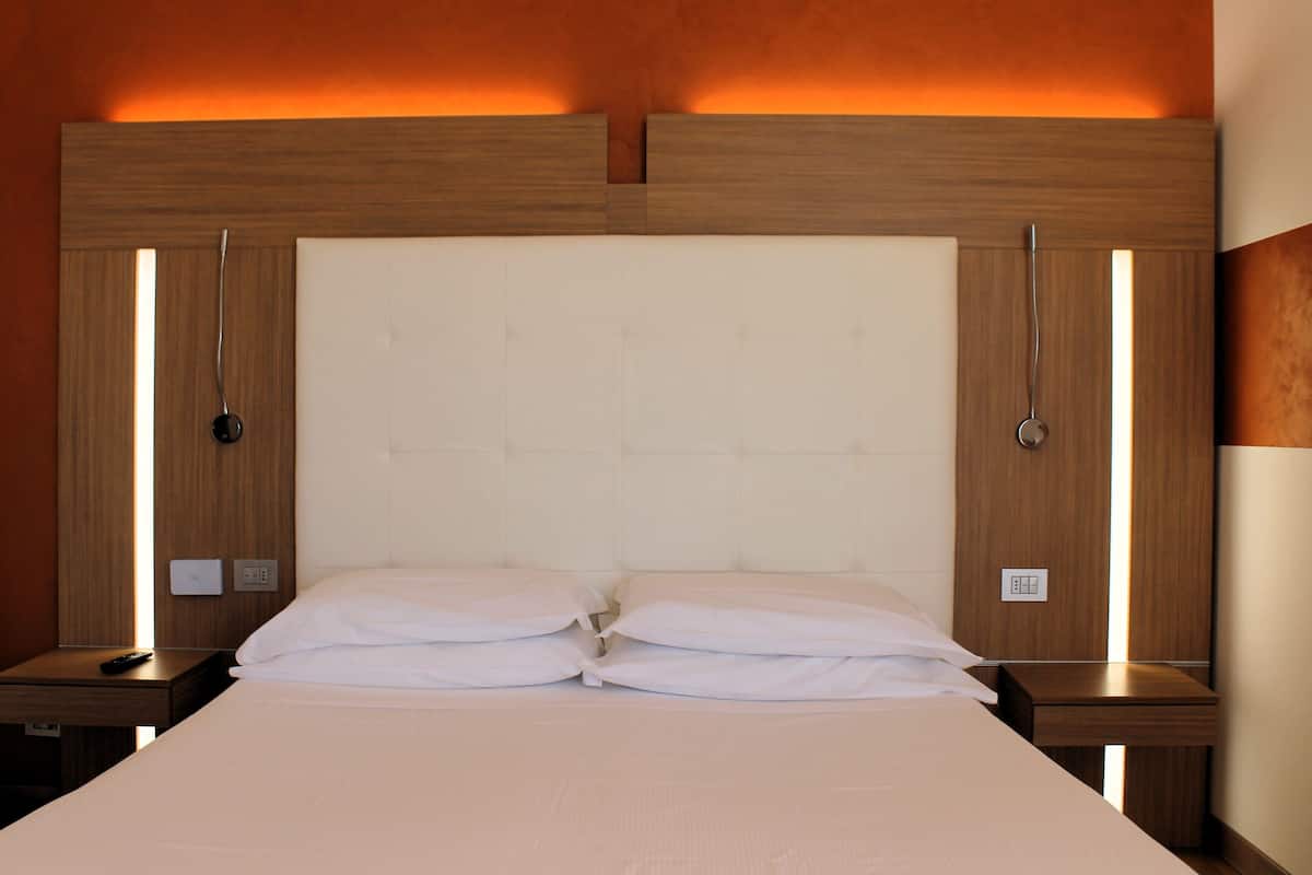 Quarto de hotel com cama grande, cabeceira de madeira, mesas de cabeceira e iluminação embutida na parede.