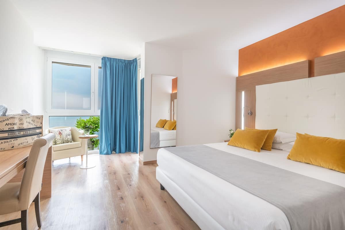 Quarto de hotel moderno com uma cama grande, uma escrivaninha, uma cadeira e vista para o exterior.
