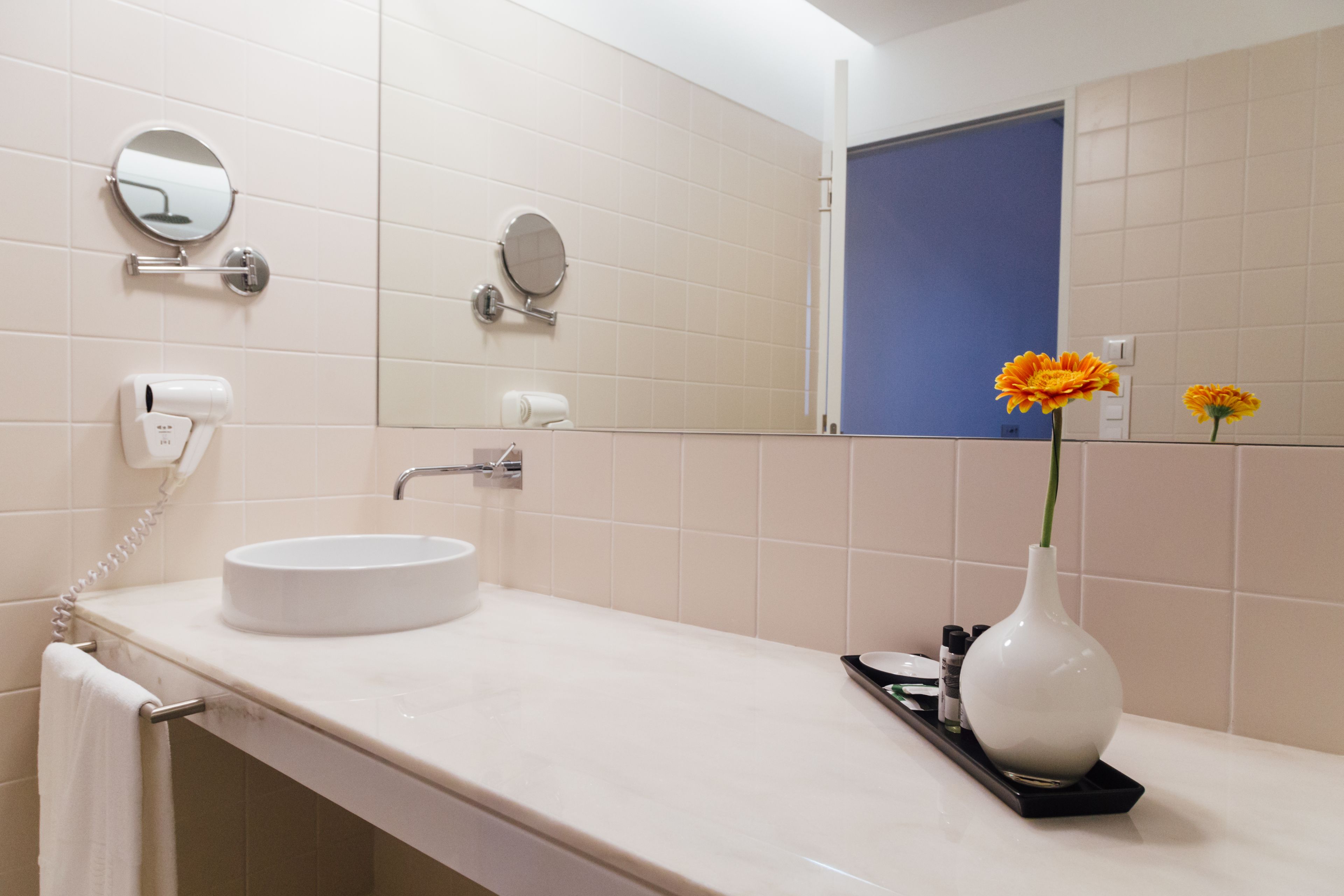 Uma casa de banho com uma pia branca, um espelho, um porta-toalhas e um vaso com flores.