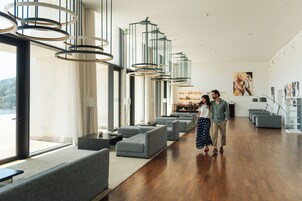 Um hall de hotel moderno com sofás cinzas, piso de madeira e uma janela grande que oferece uma vista.