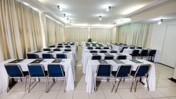 Uma sala de conferências com mesas e cadeiras dispostas em fileiras, toalhas brancas e cadeiras azuis.