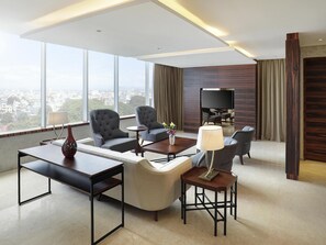 Quarto de hotel moderno com uma janela ampla, TV de tela plana e área de estar com mesa de centro e cadeiras.