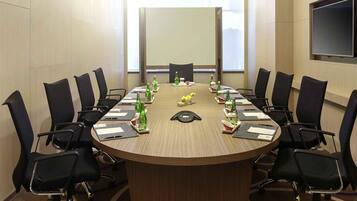 Uma sala de conferência com uma mesa comprida, cadeiras, uma tela de projetor e uma televisão.