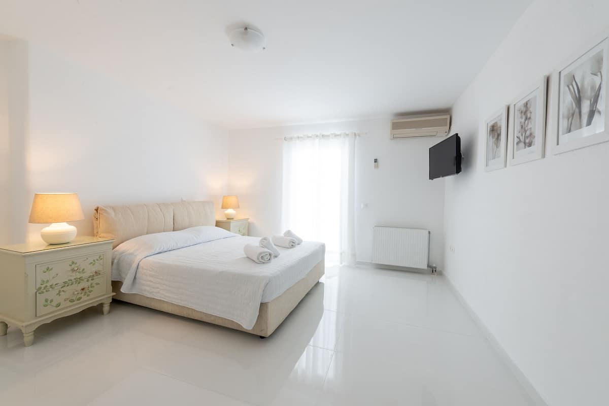Quarto com cama, abajures, penteadeira, televisão e janela com cortinas.