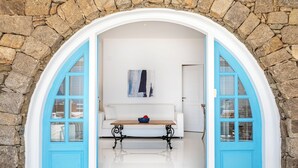 Quarto com parede de pedra, sofá branco, porta azul e um quadro na parede.