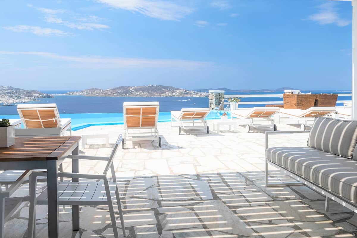 Uma área externa com assentos, piscina, cadeiras de descanso e vista para o mar.