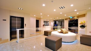 Um lobby moderno com área de estar central, balcão de recepção e cozinha visível ao fundo.