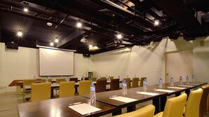 Uma sala de conferências com uma mesa comprida, cadeiras amarelas, garrafas de água e uma tela de projetor.