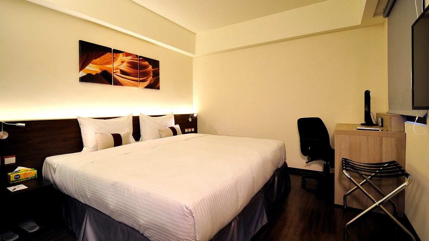 Quarto de hotel com uma cama grande, uma escrivaninha, uma cadeira, uma televisão e um quadro na parede.