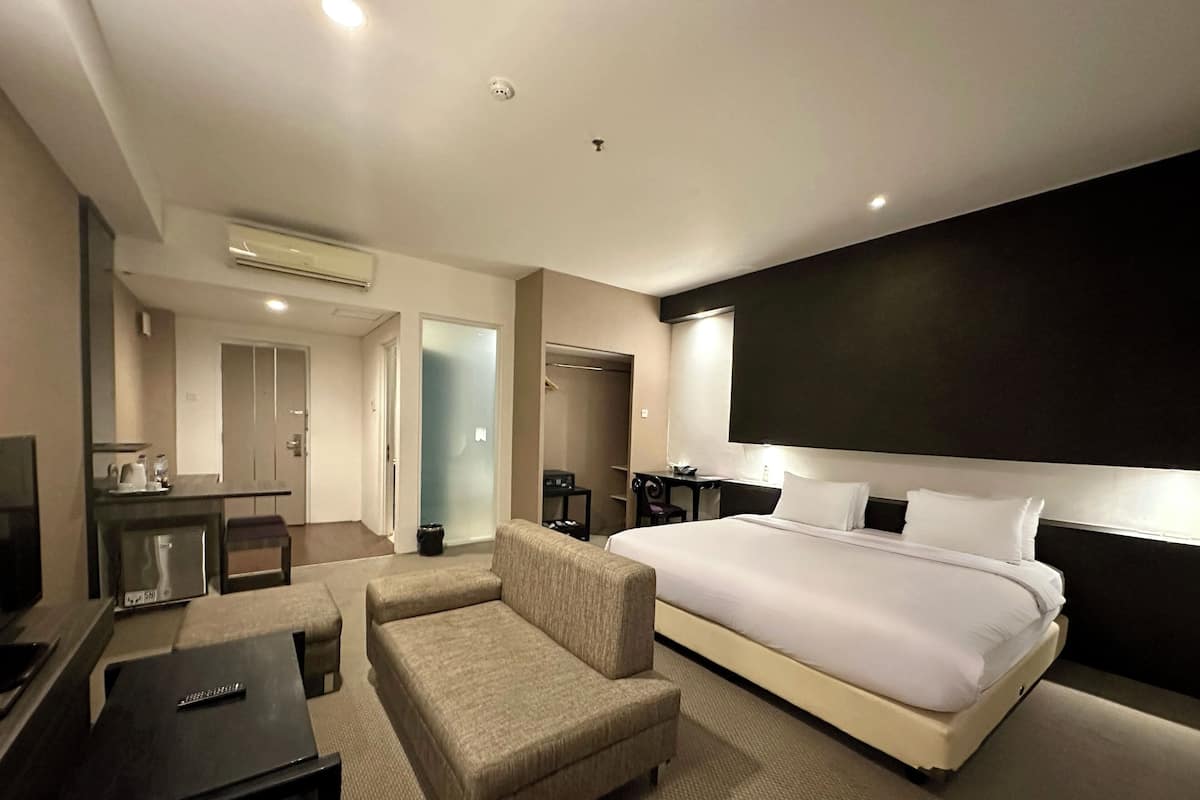Quarto de hotel com uma cama grande, uma escrivaninha, uma cadeira, uma televisão e um guarda-roupa.