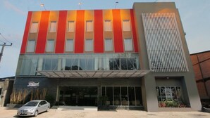 Um hotel moderno com fachada vermelha e bege, grandes janelas e entrada coberta.