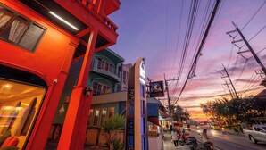 Vista da rua com edifícios, fios de eletricidade e um céu ao pôr do sol.
