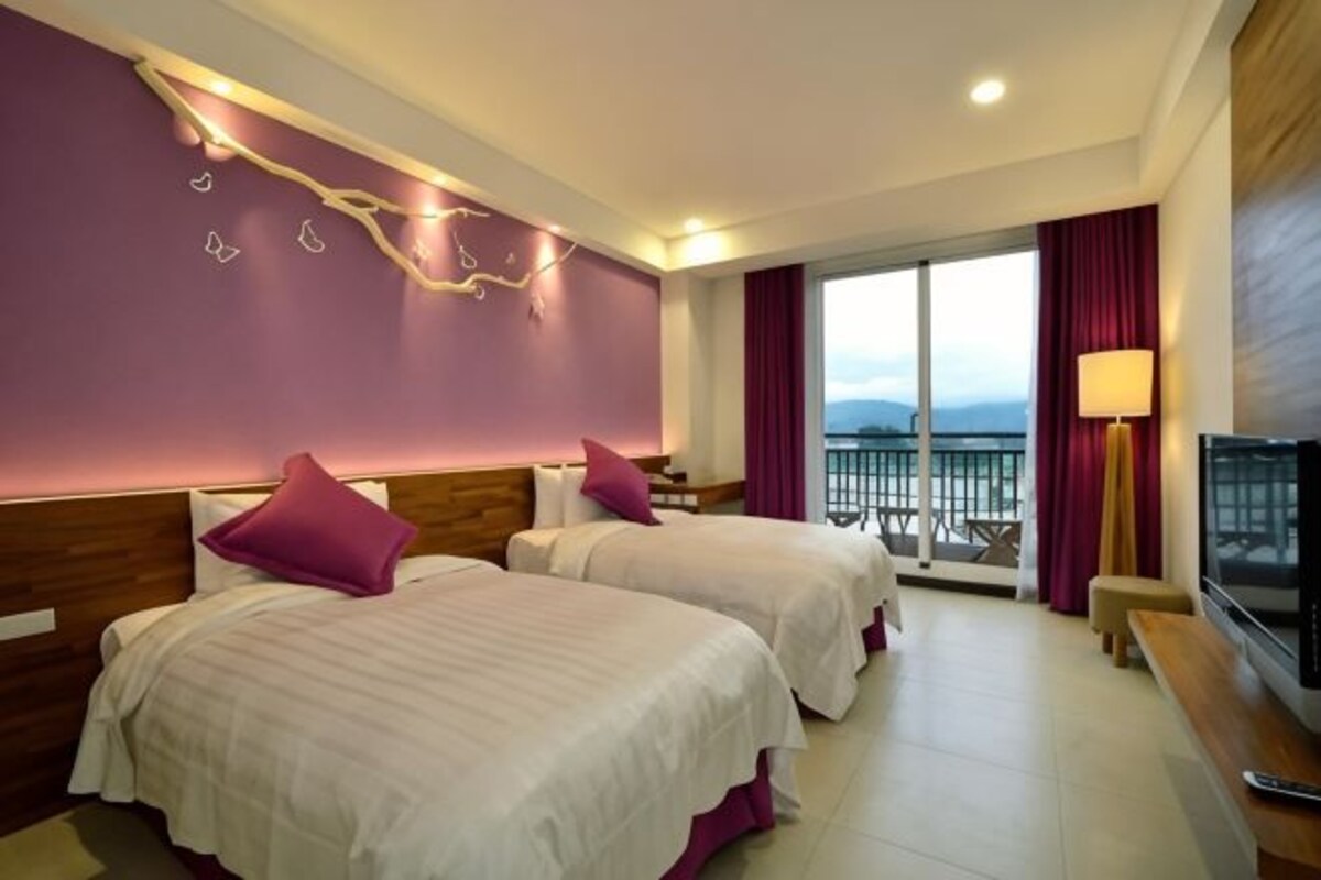 Quarto de hotel com duas camas, televisão e varanda com vista.