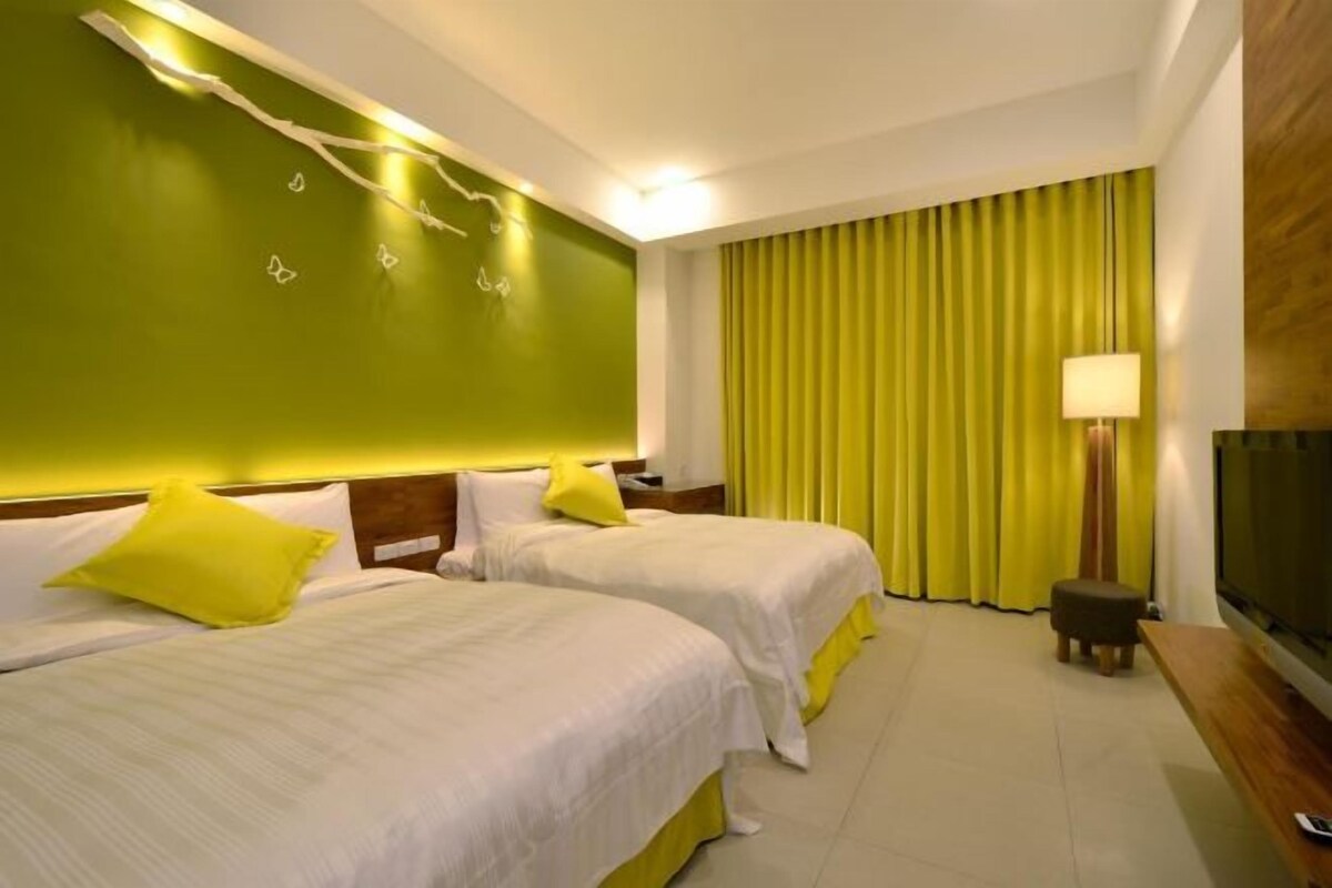 Quarto de hotel com duas camas, uma televisão e um abajur.