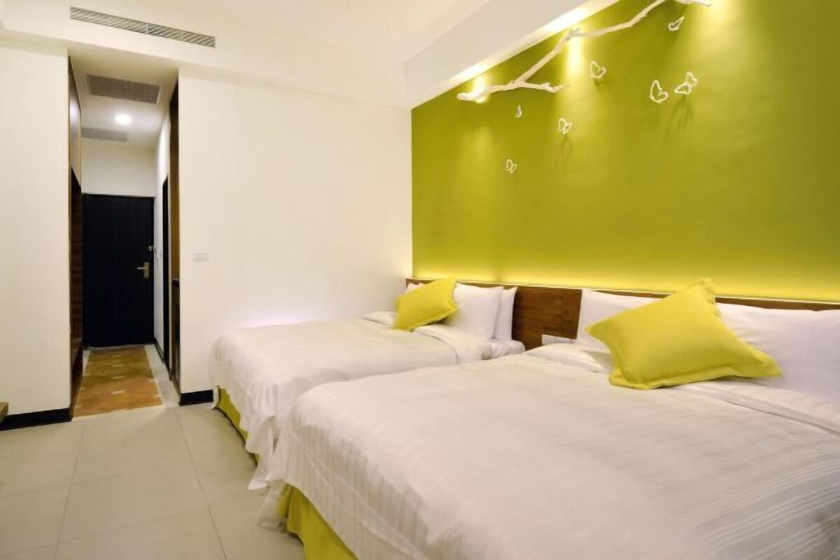 Quarto de hotel com duas camas, uma parede verde decorativa e um corredor que leva a uma porta.