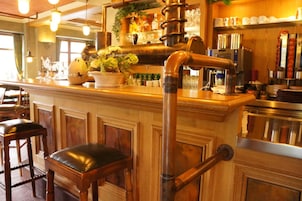 Uma área de bar com painéis de madeira, cano de cobre, banquetas e um vaso de plantas.