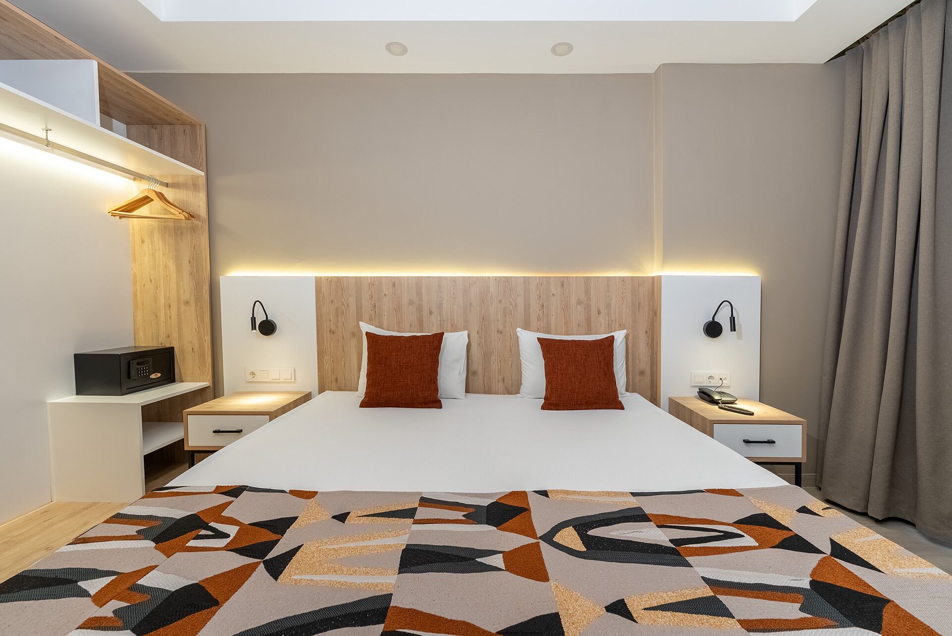 Quarto de hotel moderno com uma cama grande, duas mesas de cabeceira, um guarda-roupa embutido e uma luminária no teto.
