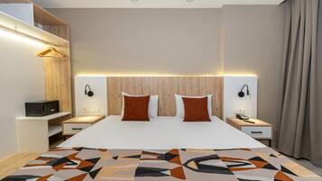 Quarto de hotel moderno com uma cama grande, duas mesas de cabeceira, um guarda-roupa embutido e uma luminária no teto.