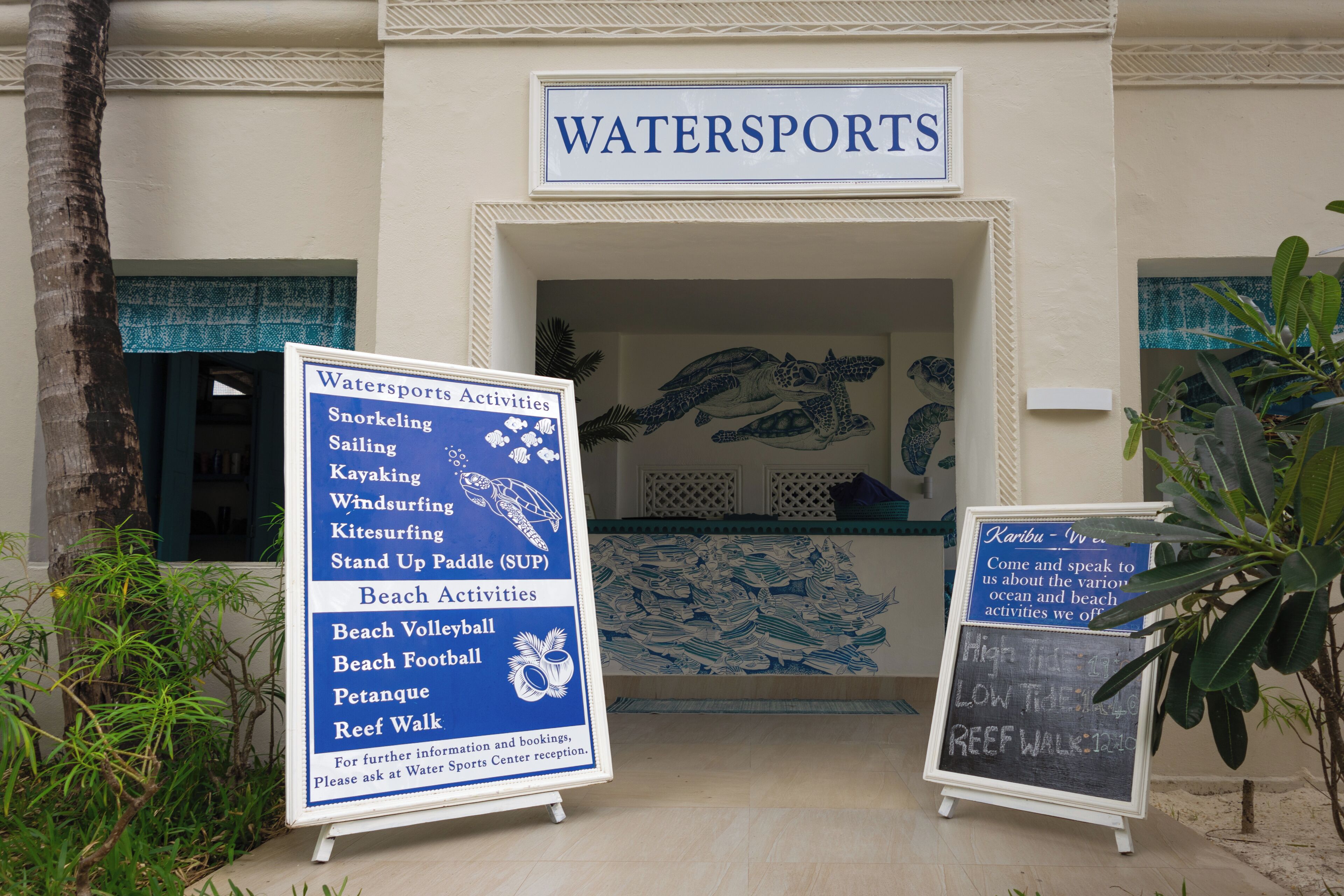 Placa listando atividades esportivas aquáticas e placa com atividades de praia em uma localização à beira-mar.